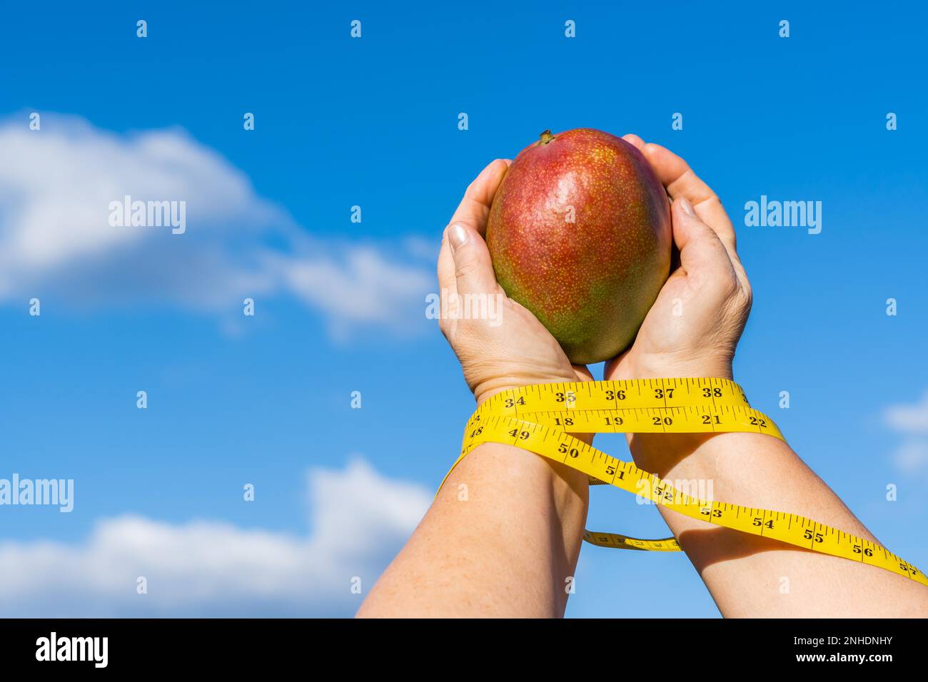 Woman holding a mango in her hands with a tape measure and a sky with ...