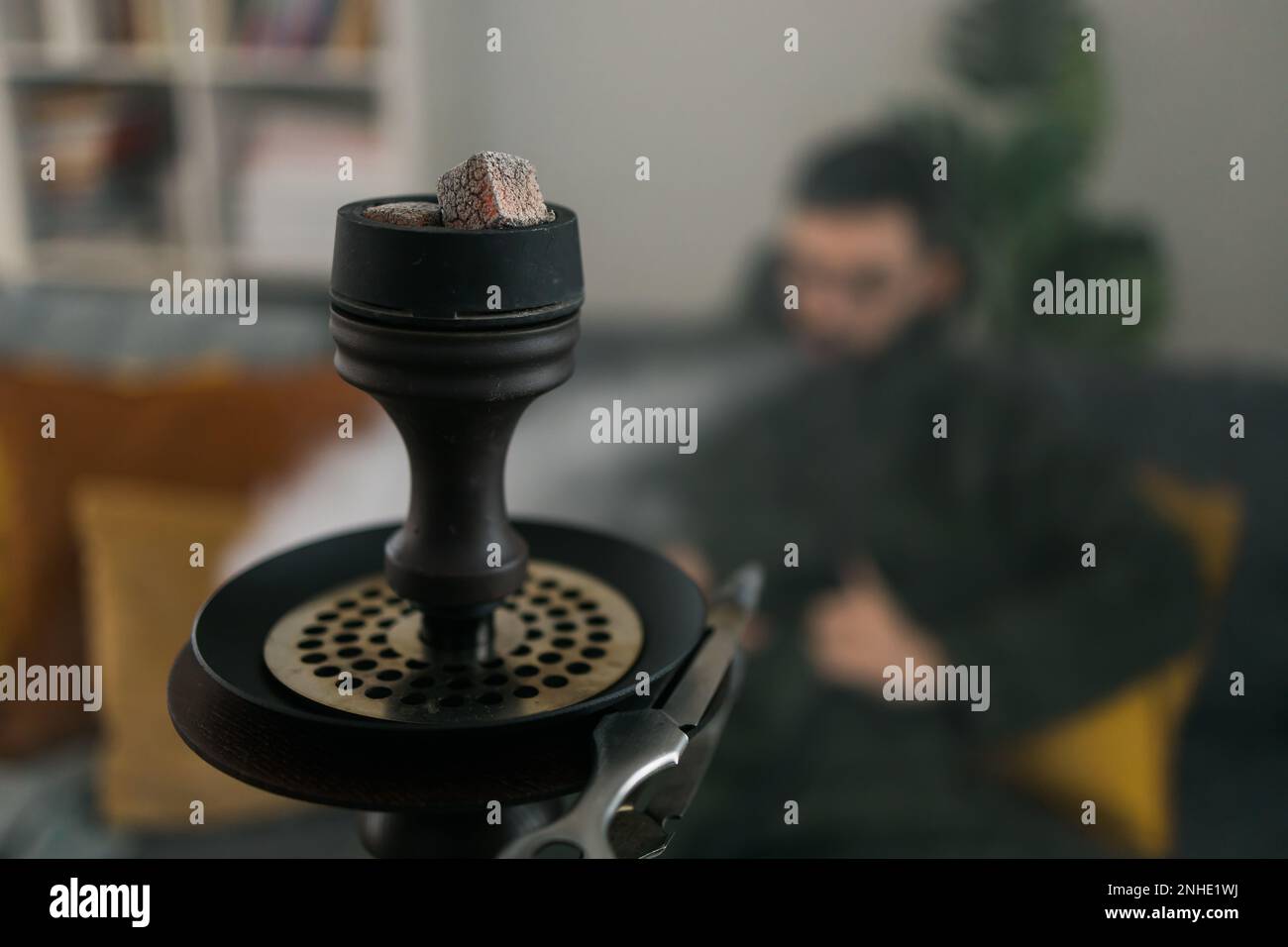 Hookah shisha with glass flask and metal bowl in room with man ...