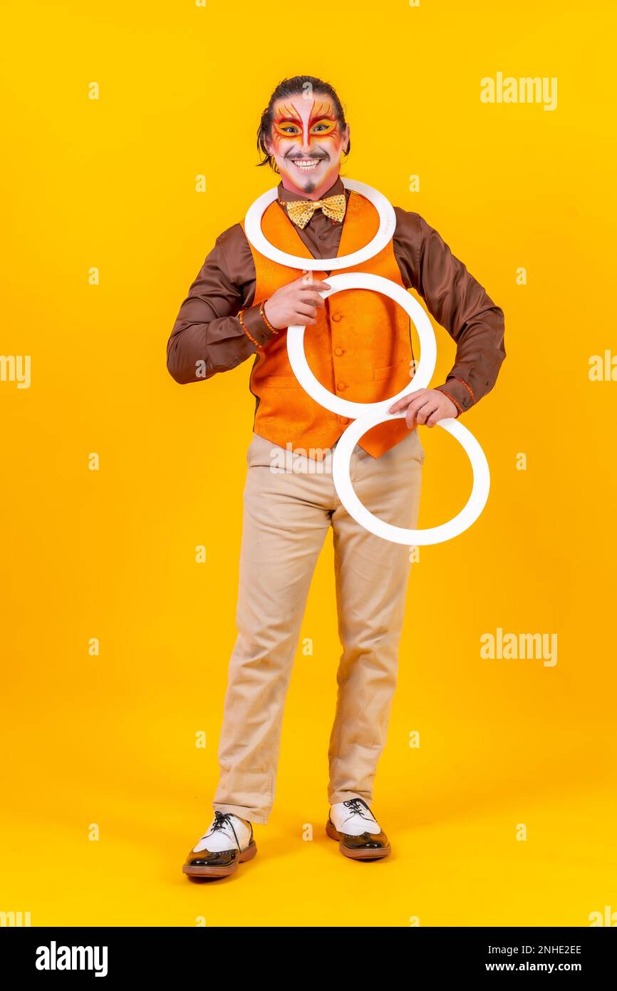 Happy juggler man in makeup vest juggling hoops on a yellow background ...