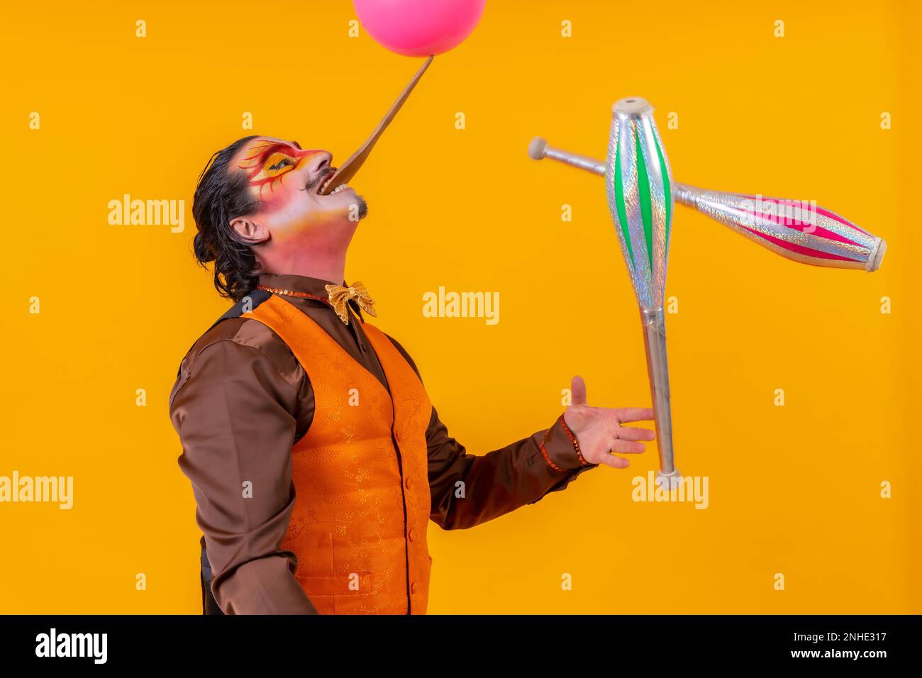 Portrait of a juggler in a vest with a painted face juggling with maces ...