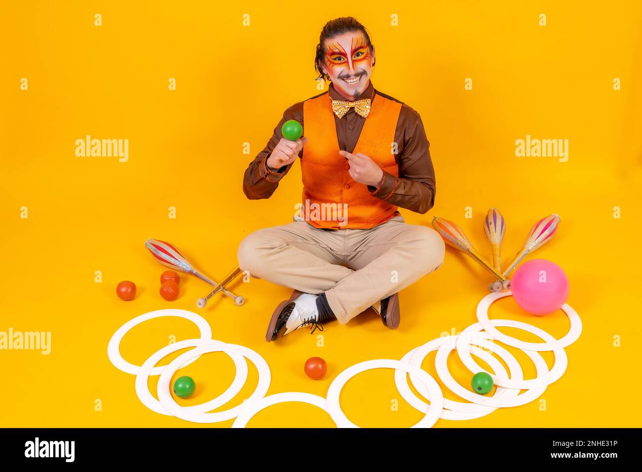 Portrait of a juggler in a vest and makeup sitting with the objects on ...