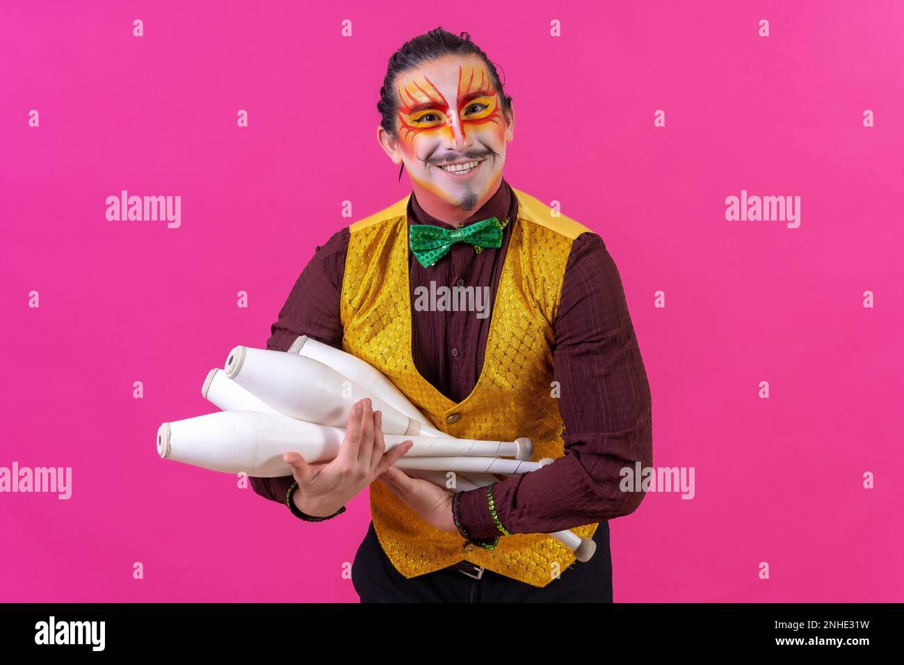 Juggler in a vest and with painted face juggling clubs on a pink ...