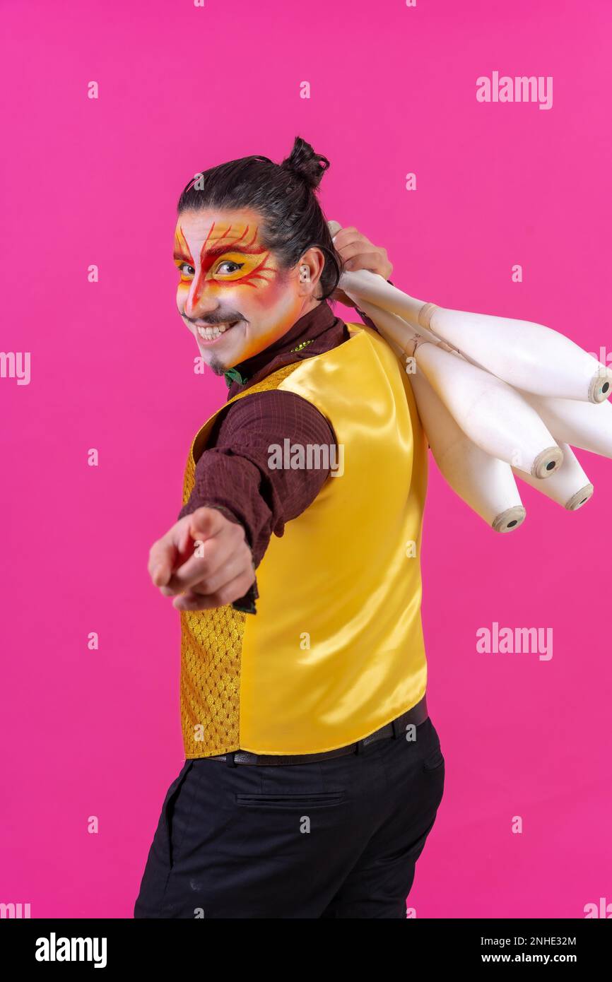 Juggler in a vest and with painted face juggling maces on a pink ...