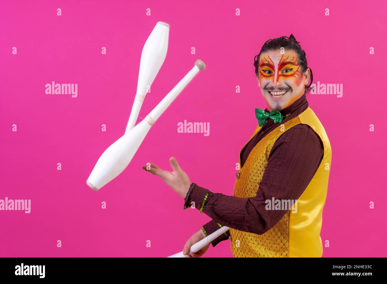 Clown with white facial makeup on a pink background, smiling juggling ...