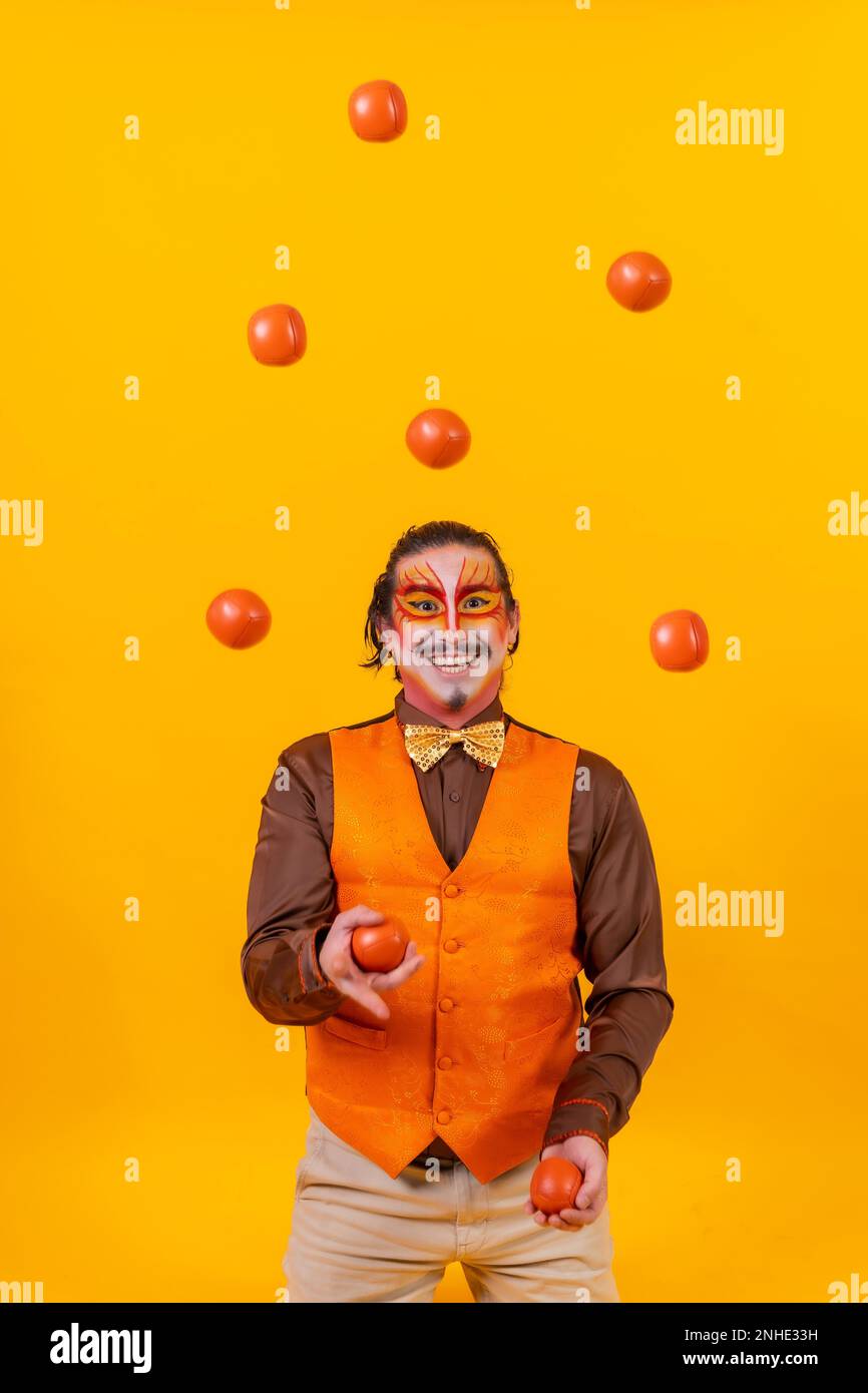 Juggler in a vest and with a painted face juggling balls on a yellow ...