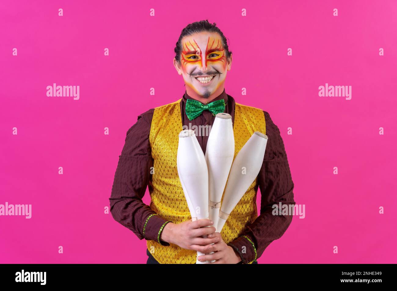 Juggler in a vest and with painted face juggling maces on a pink ...