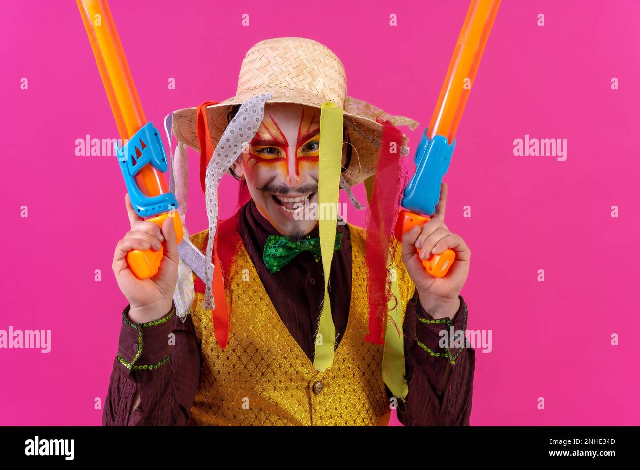 Clown with white facial makeup on a pink background, with toy guns and ...