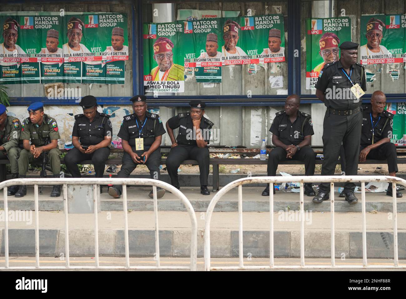 Nigerian police officers sit under campaign posters of Bola Ahmed ...