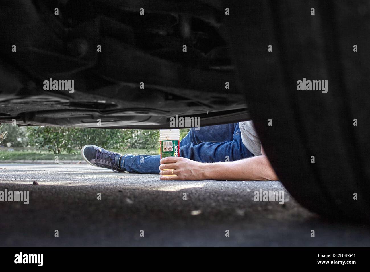 A mechanic on the ground, we can see his leg and arm holding a product ...