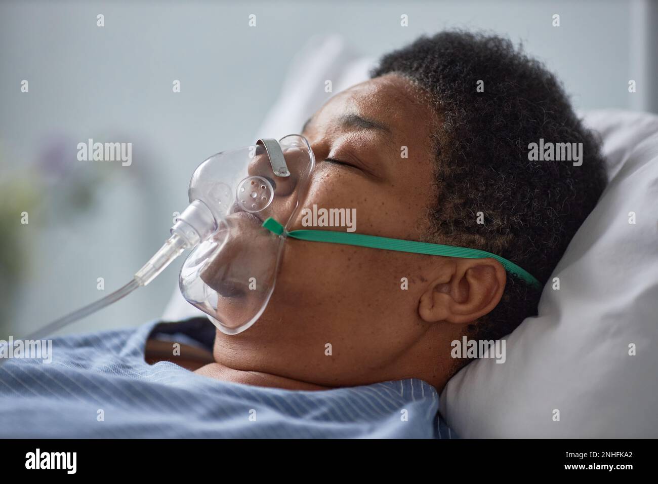 Side view closeup of black senior woman sleeping on bed in hospital room with oxygen support ...
