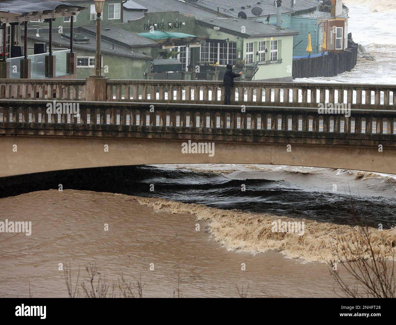 A storm surge wave crests under the Stockton Avenue Bridge as it flows ...