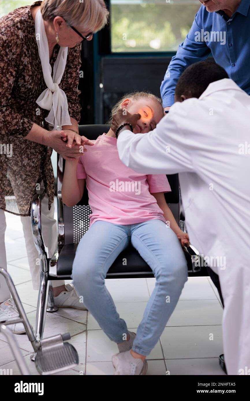 Practitioner doctor shining light into little girl patient eye while ...