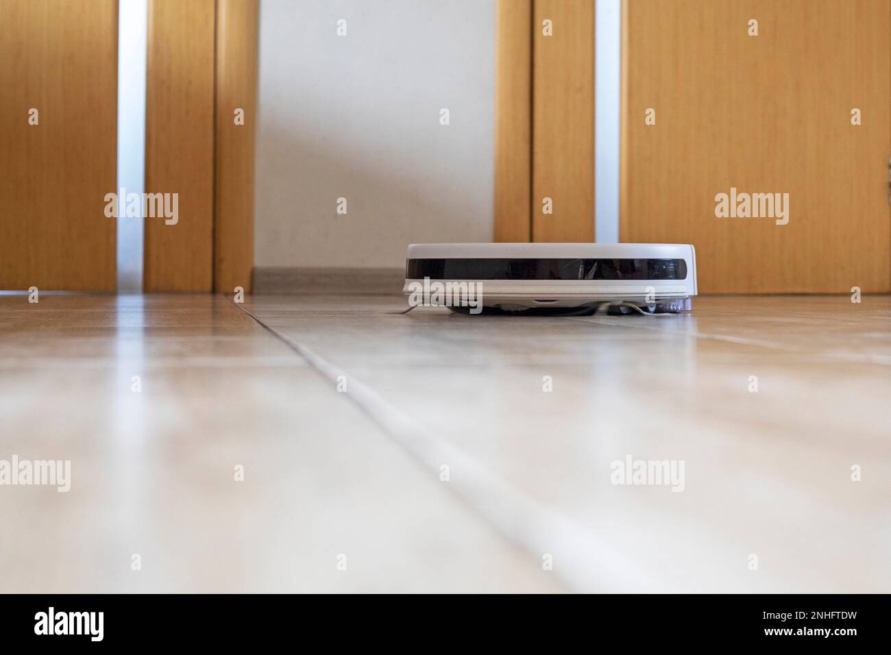 white robot vacuum cleaner cleans the room near the oak doors ...