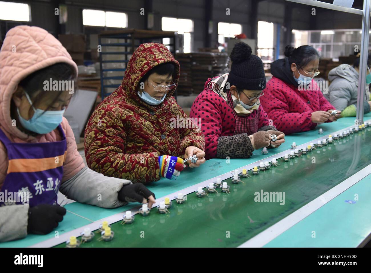 Workers bundled against the cold weather assemble speakers at an ...