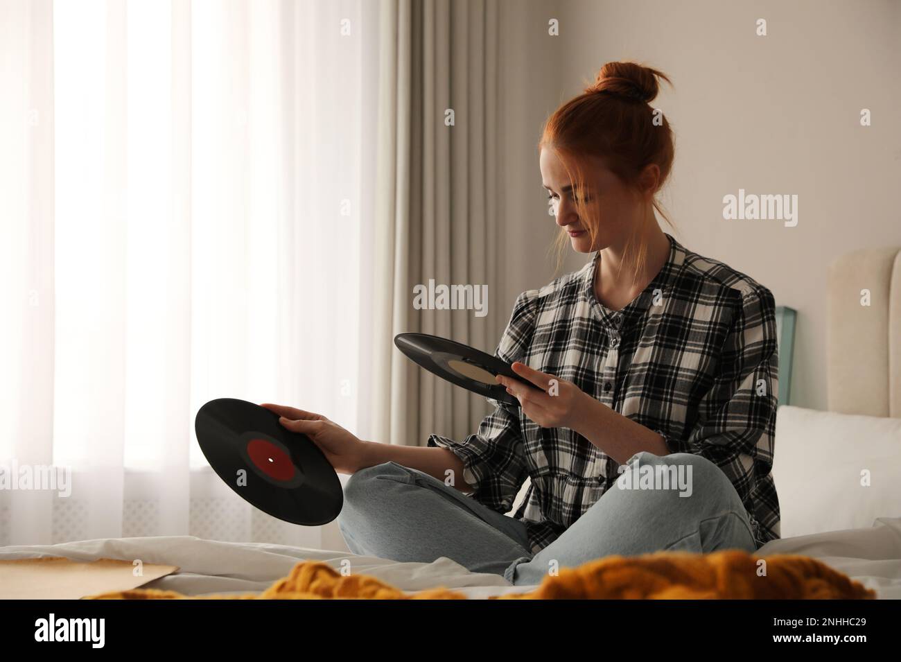 Young woman choosing vinyl disc to play music with turntable in bedroom ...