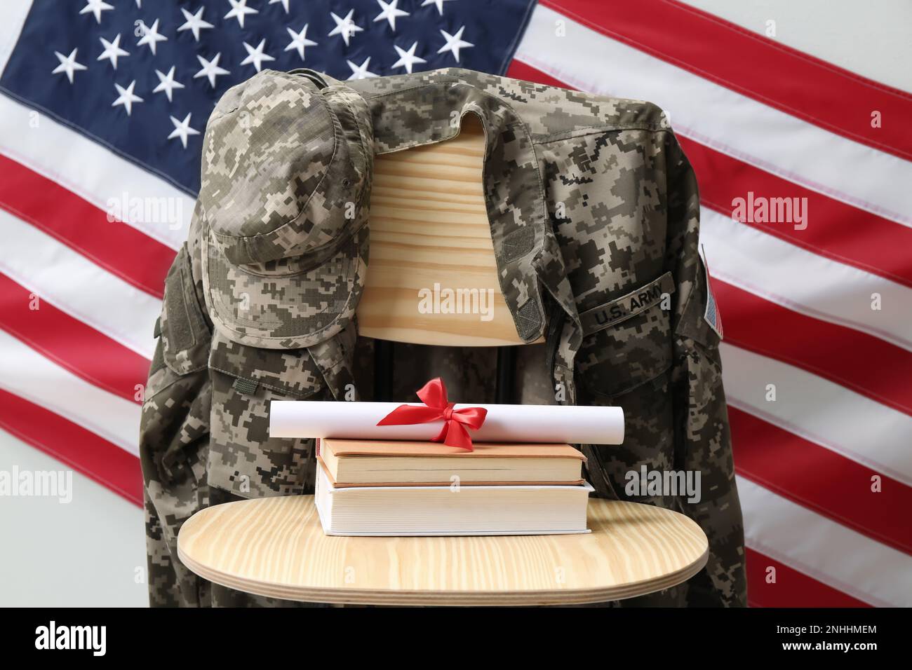Diploma, books and soldier uniform on wooden chair near flag of United ...