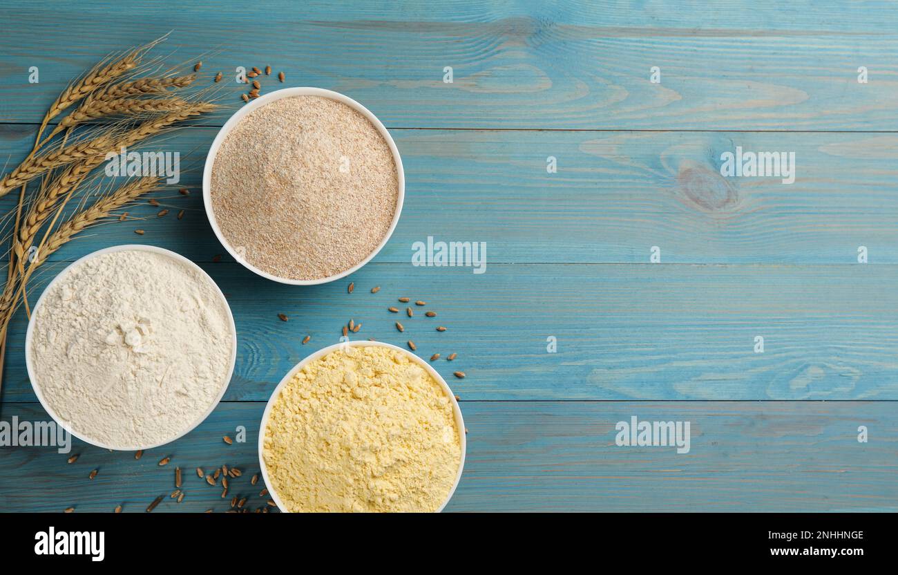 Different types of flours and wheat ears on light blue wooden table ...