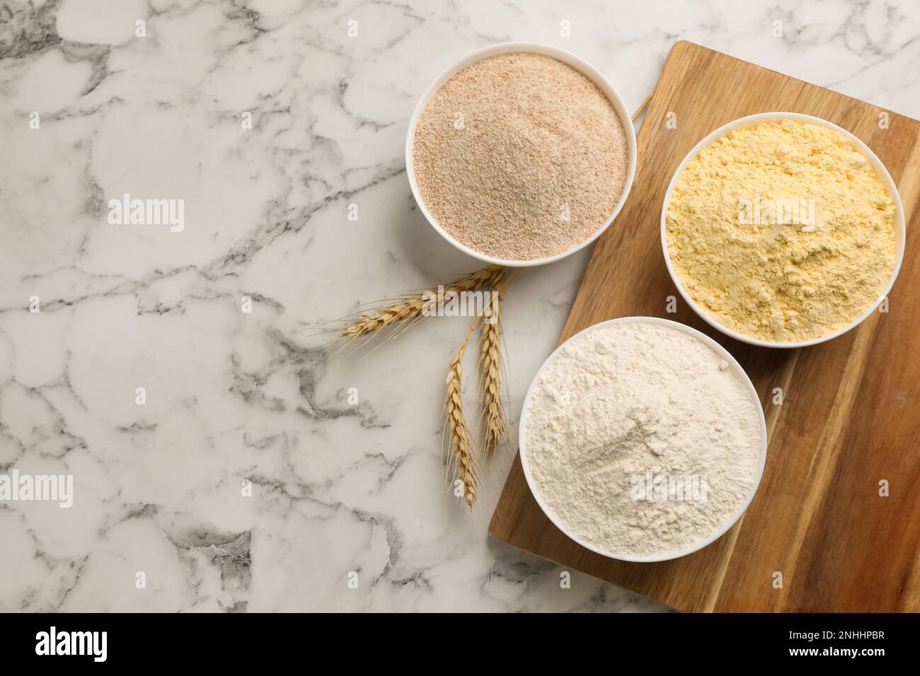 Different types of flours and wheat ears on white marble table, flat ...