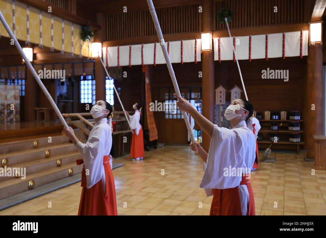 Miko, Shrine maiden, wearing face masks perform a susuharai by bamboo ...
