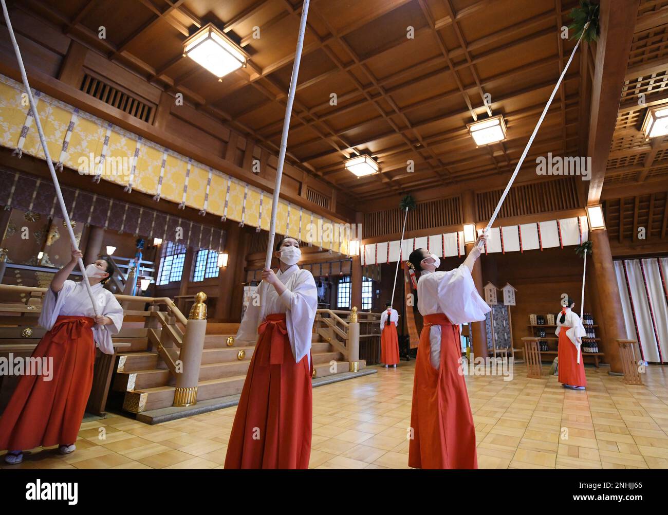 Miko, Shrine maiden, wearing face masks perform a susuharai by bamboo ...