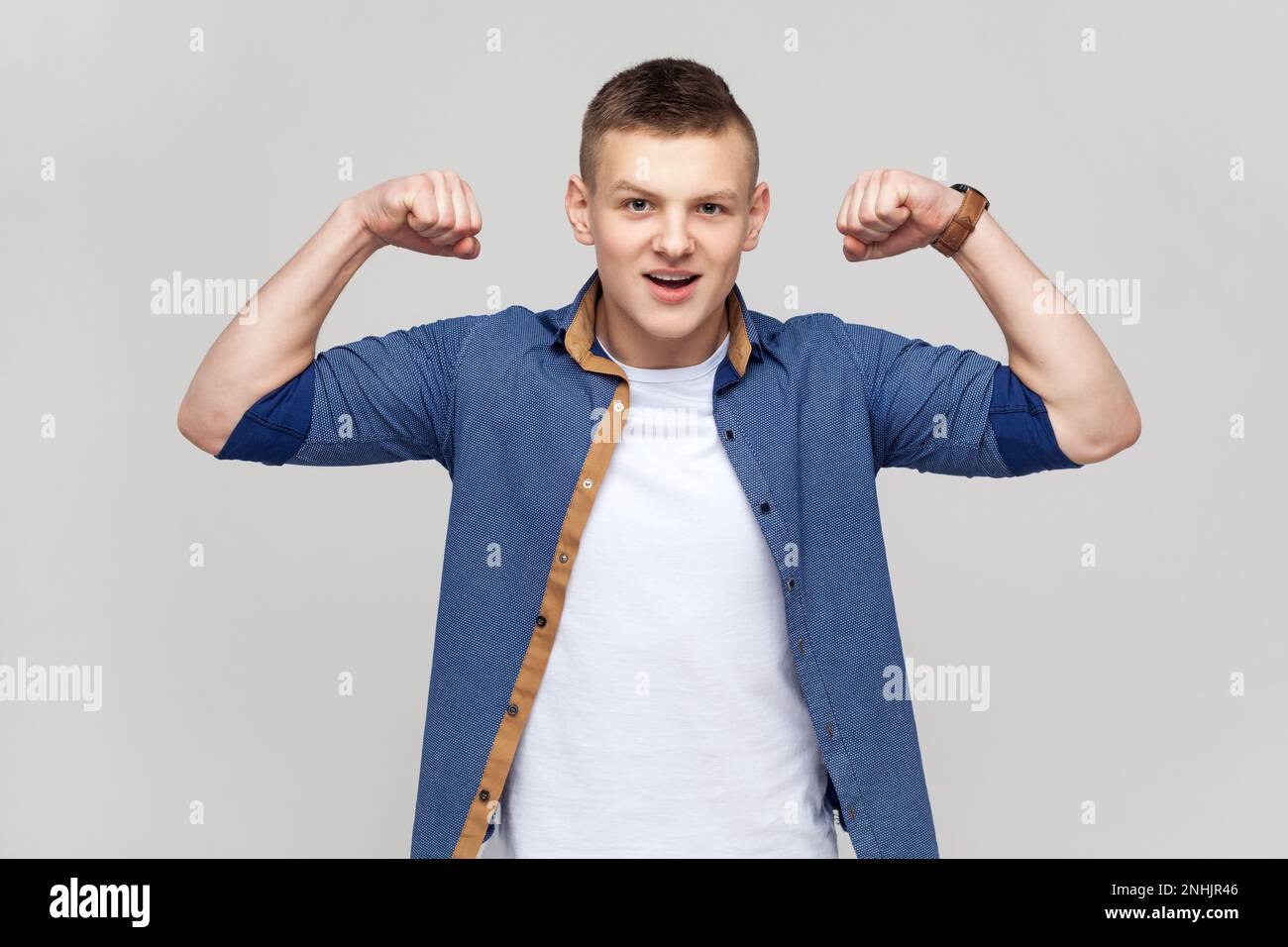 Portrait of strong teenager boy wearing blue shirt demonstrating power ...