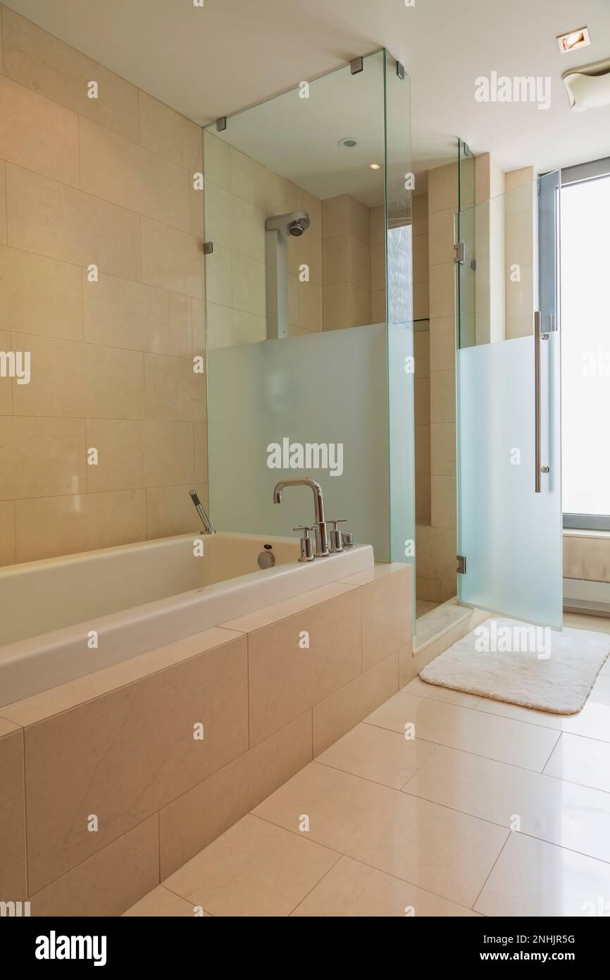 White bathtub in marble casing and glass shower stall in bathroom with marble tile floor inside ...