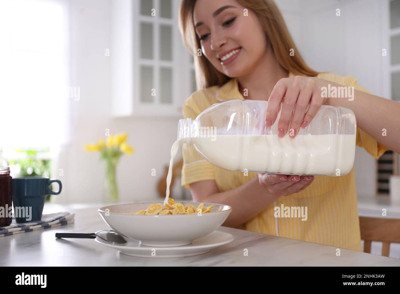 Young woman pouring milk from gallon bottle into plate with breakfast ...