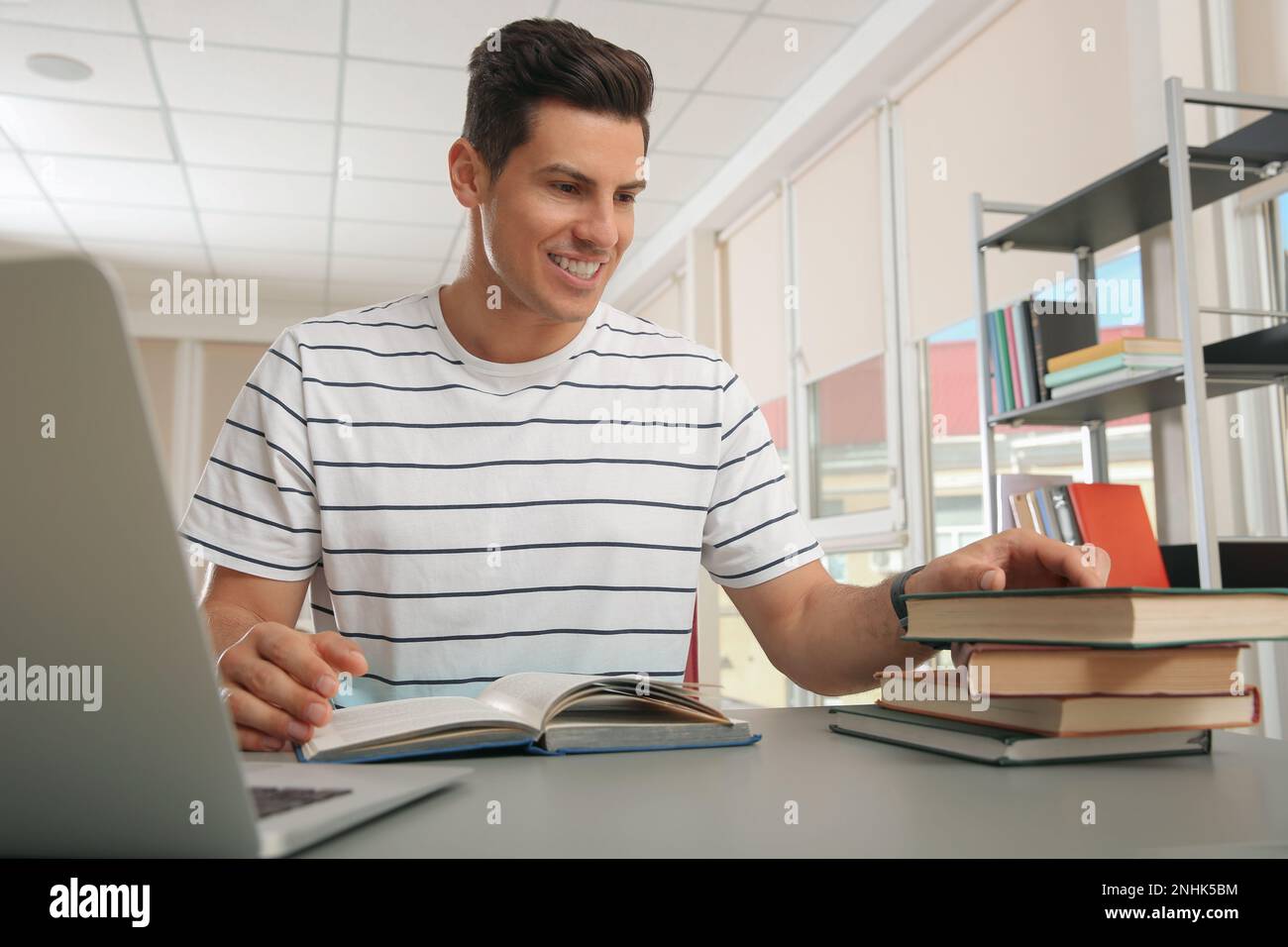 Man with laptop and books studying at table in library Stock Photo - Alamy