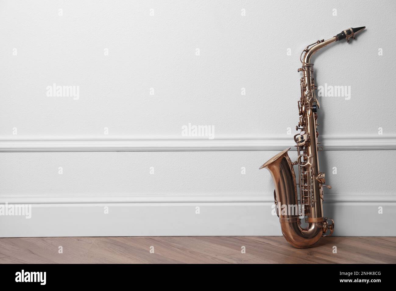 Beautiful saxophone on floor near white wall indoors, space for text ...