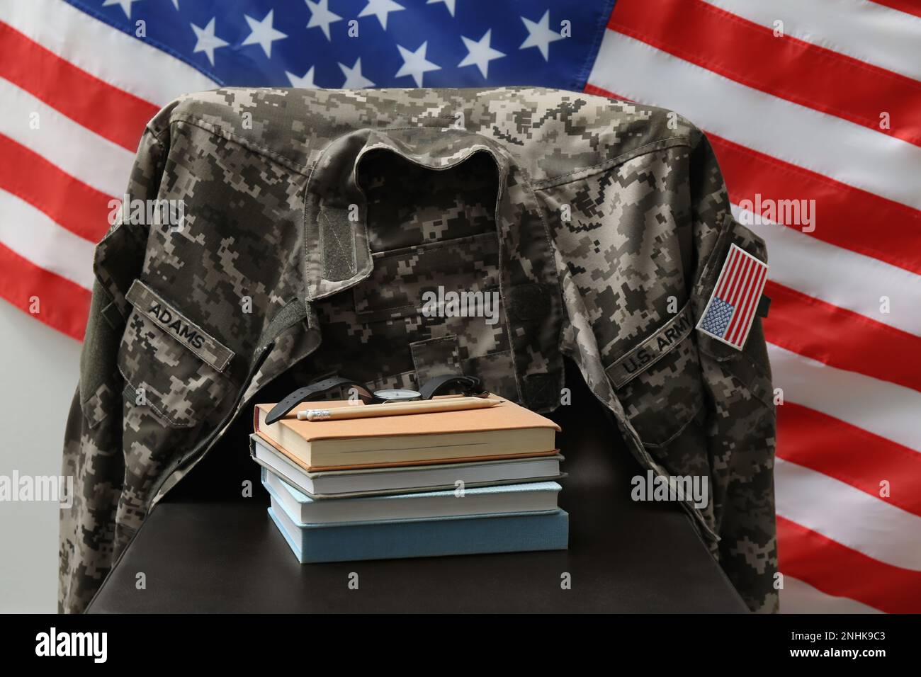 Books, watch and soldier uniform on chair near flag of United States ...