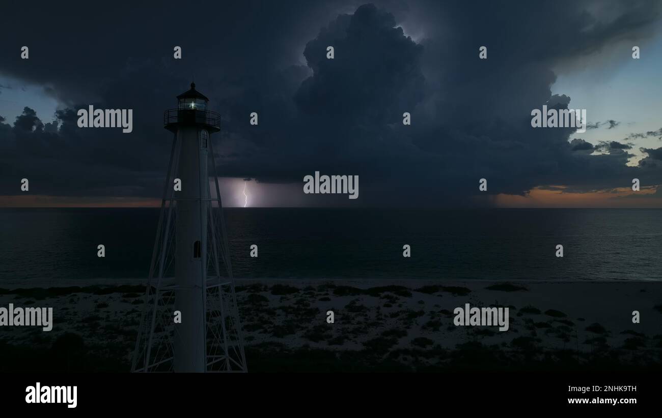 White tall lighthouse on sea shore with blinking light at stormy night ...