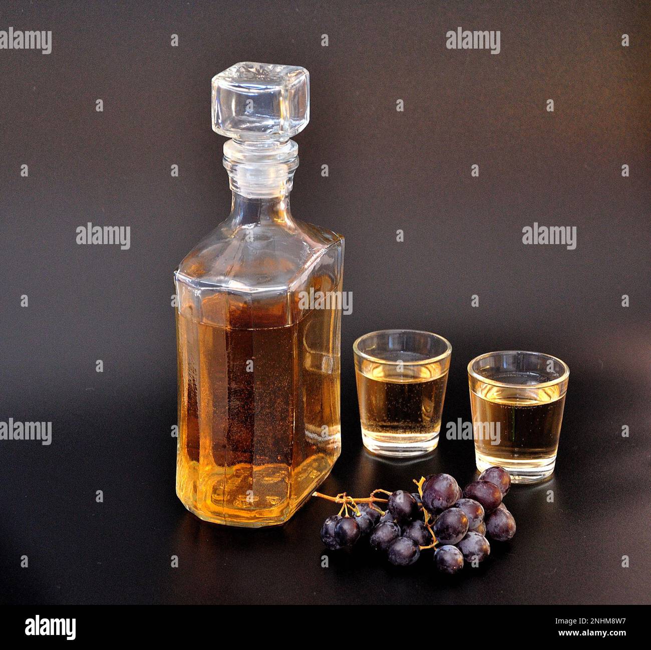 Grappa, traditional Italian alcohol in two glasses and a glass decanter with a bunch of dark ...