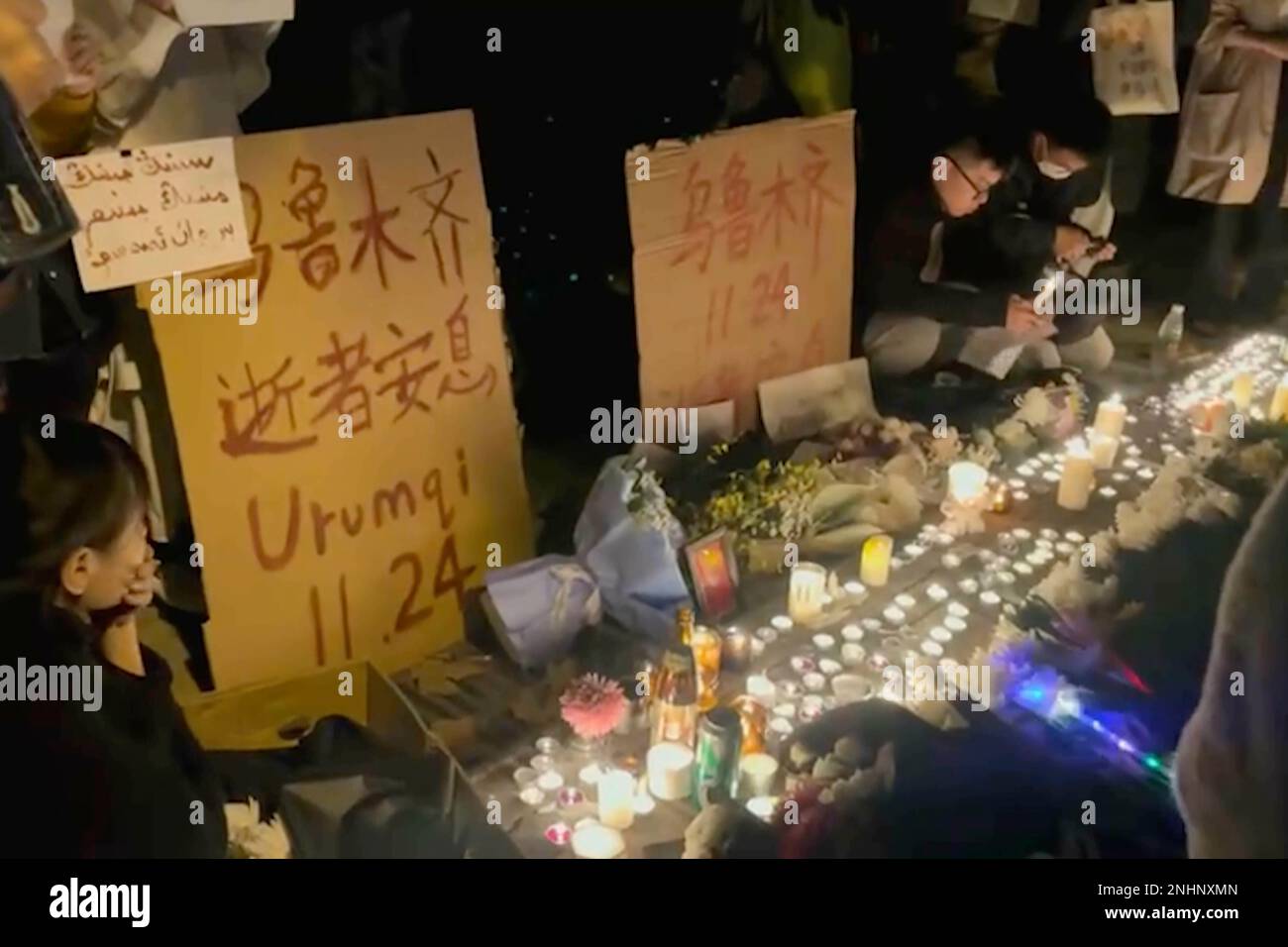 Residents light candles near a sign which reads "Urumqi, 11.24, Rest in ...