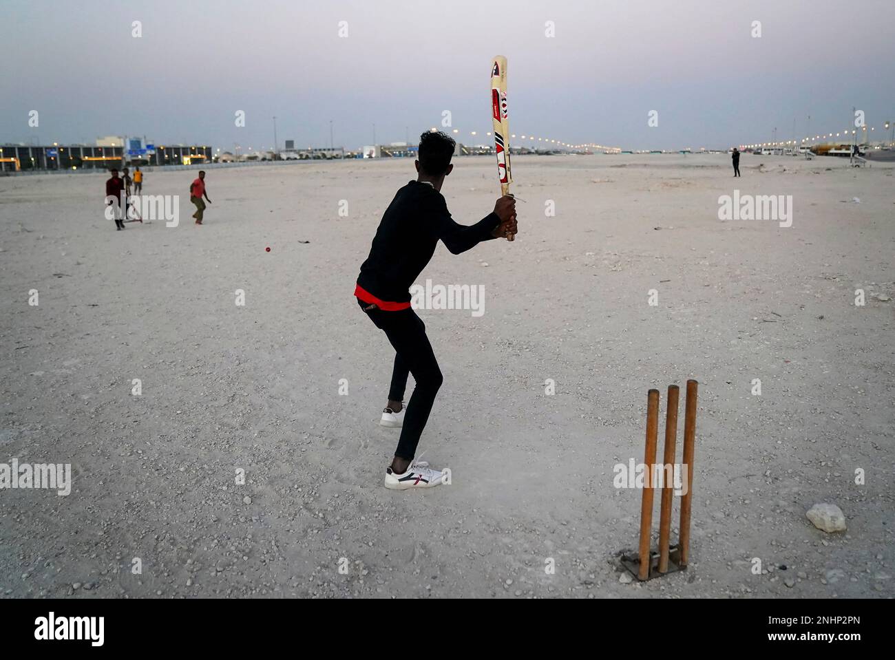 Migrant workers play cricket before watching soccer on a big projection ...