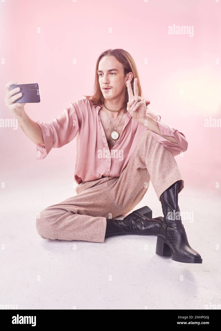 Selfie, peace and fashion with a gay man in studio on a pink background ...