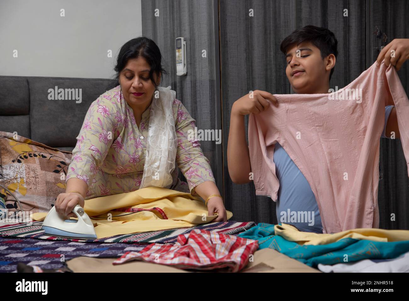 Mother ironing shirt on bed and her son standing beside Stock Photo - Alamy