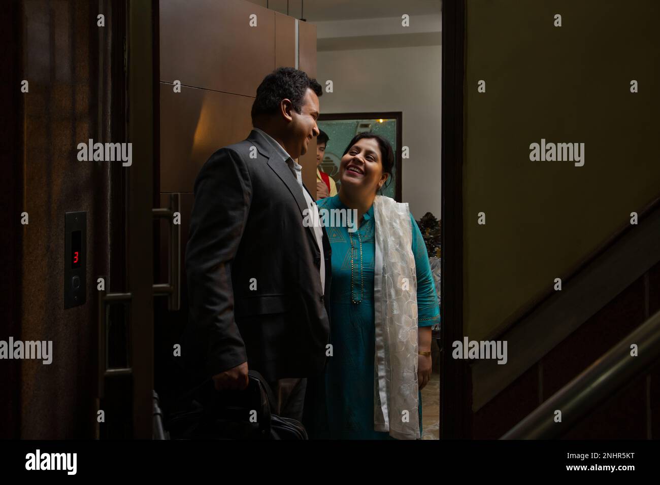 Woman saying goodbye to her husband at the door while going to office ...