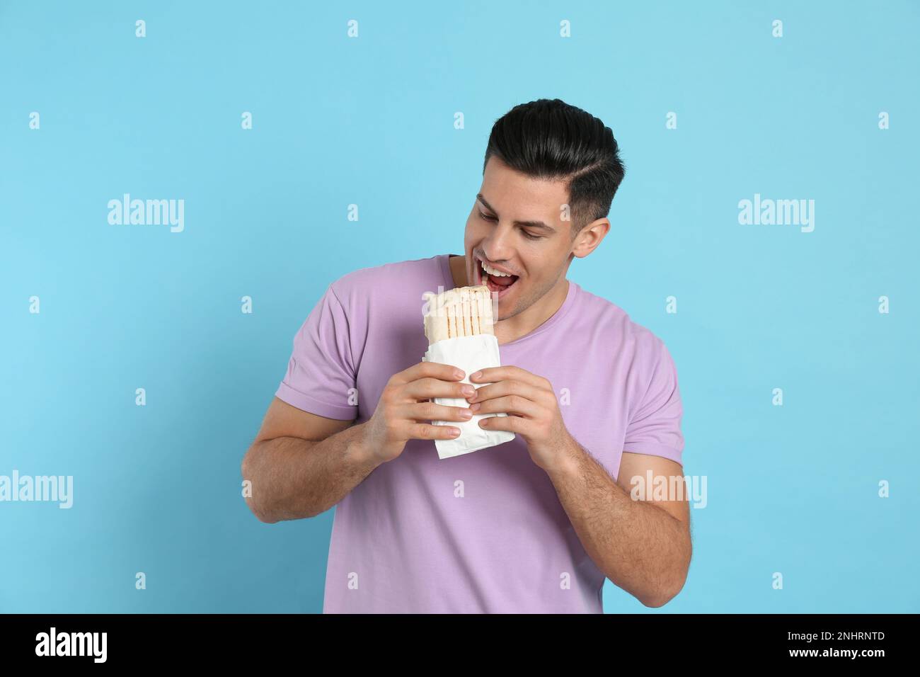Man eating delicious shawarma on turquoise background Stock Photo - Alamy