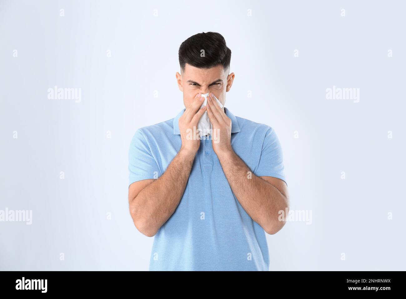 Man with tissue suffering from runny nose on white background Stock ...