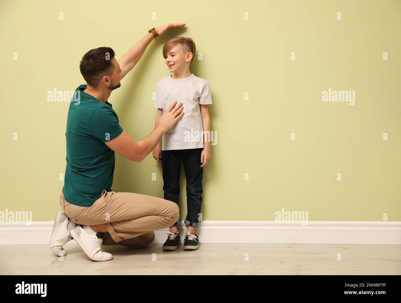 Father measuring height of his son near light wall indoors. Space for ...