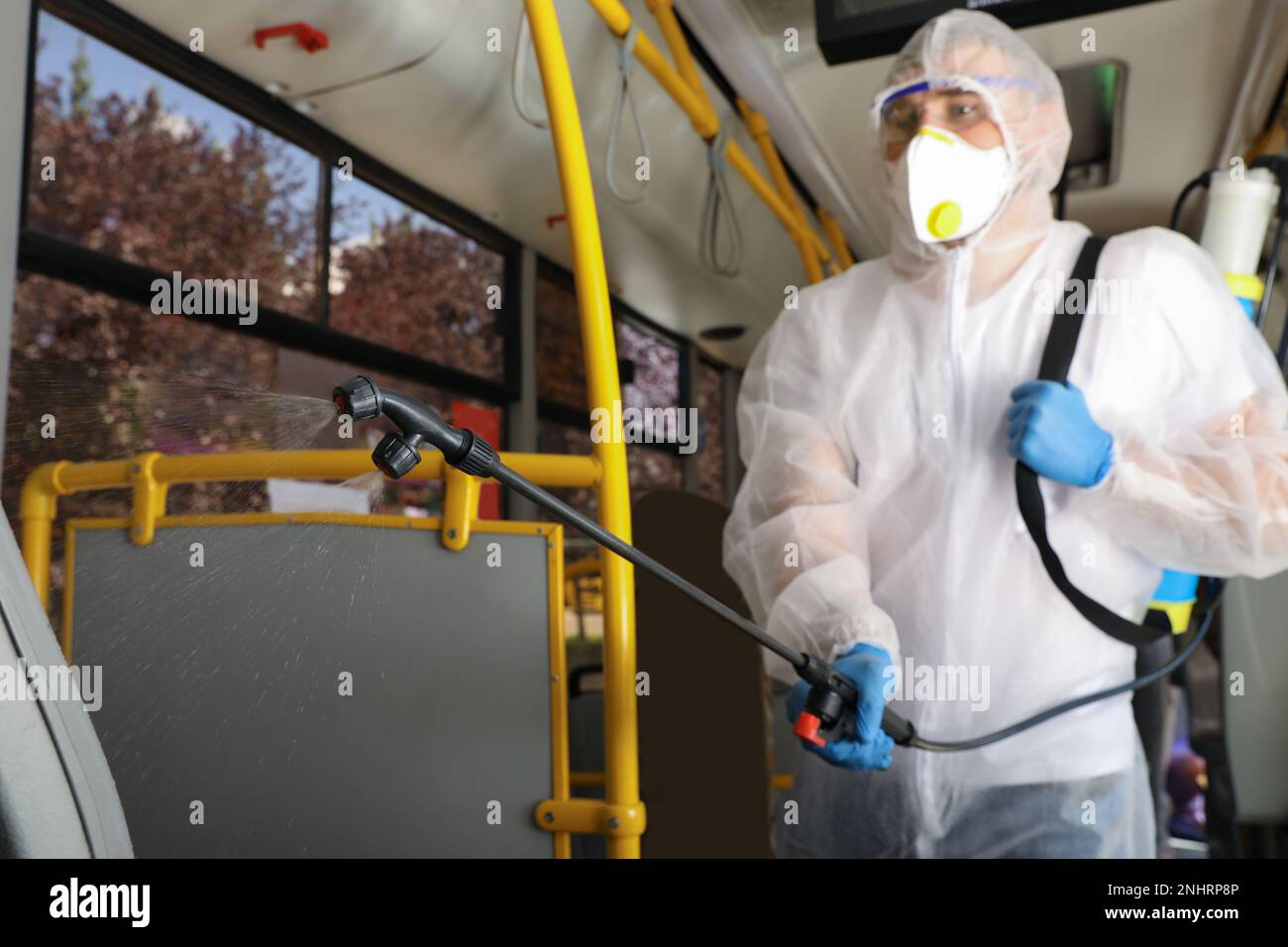 Public transport sanitation. Worker in protective suit disinfecting bus ...