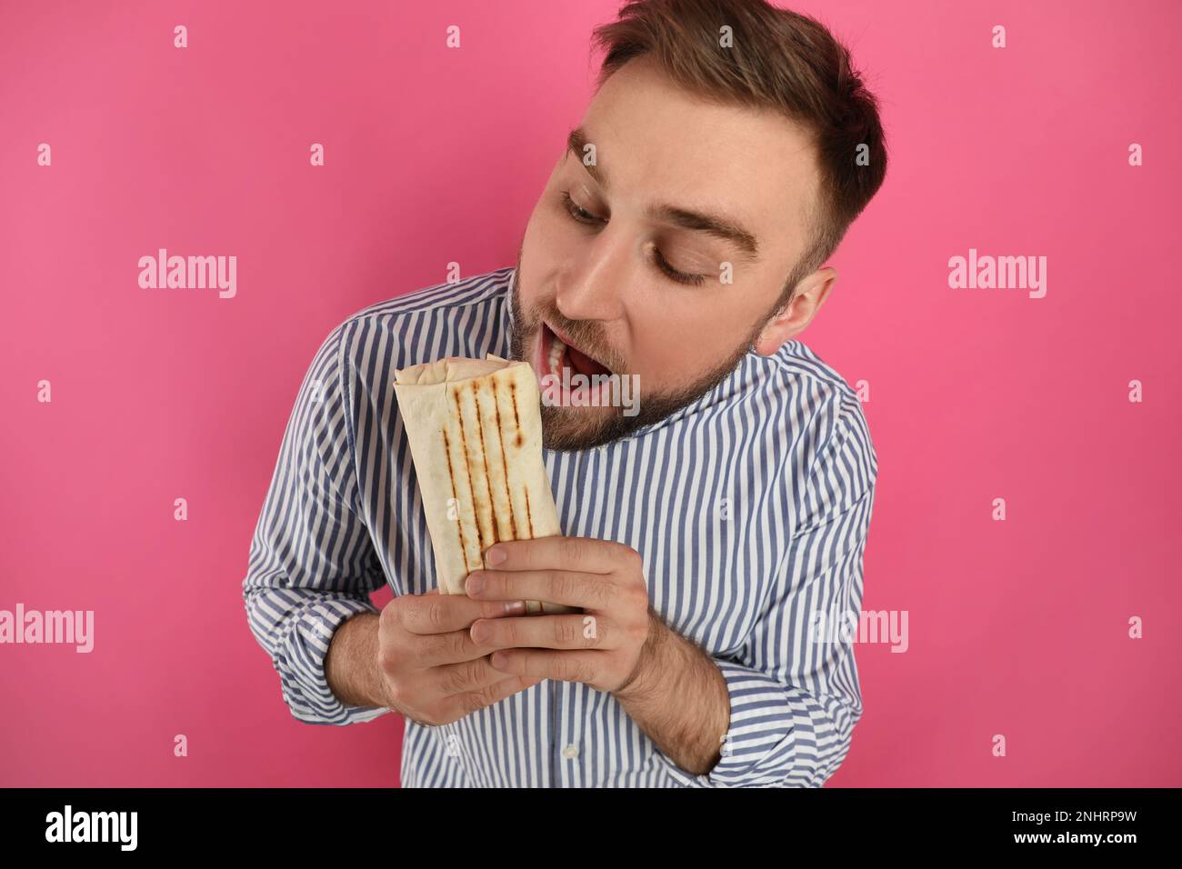 Young man eating delicious shawarma on pink background Stock Photo - Alamy