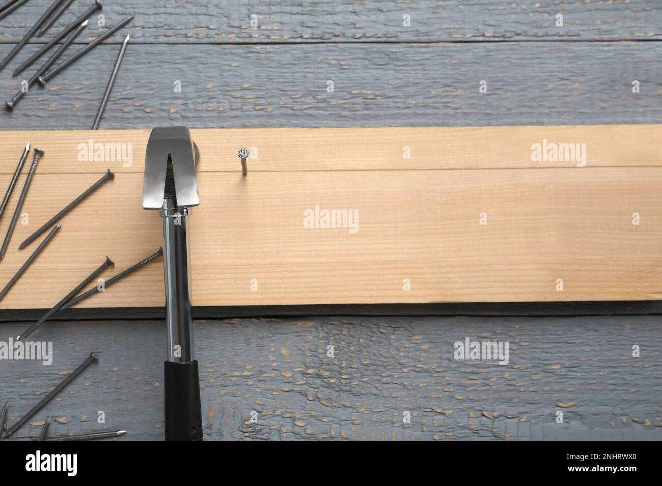 Hammering nails into plank on grey wooden table, flat lay. Space for ...