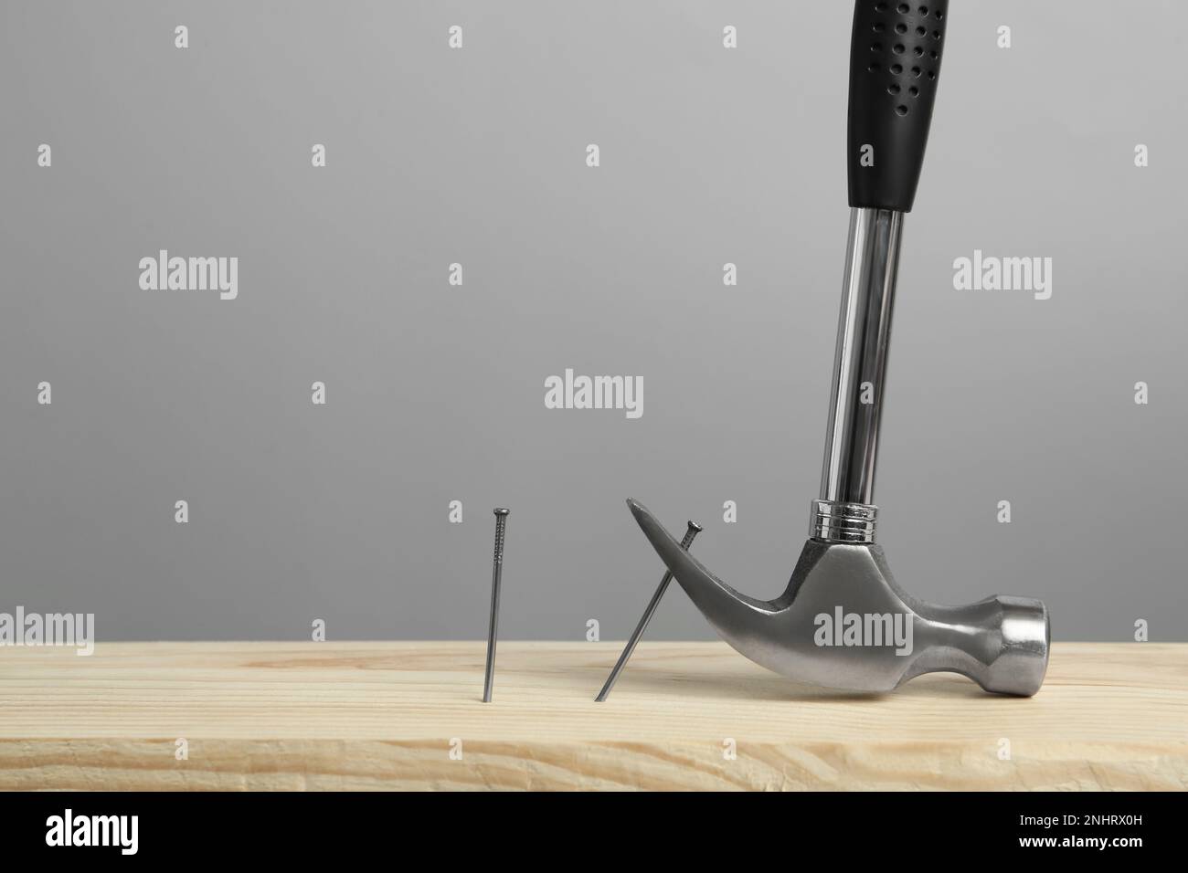 Hammer pulling metal nail out of wooden surface against grey background ...