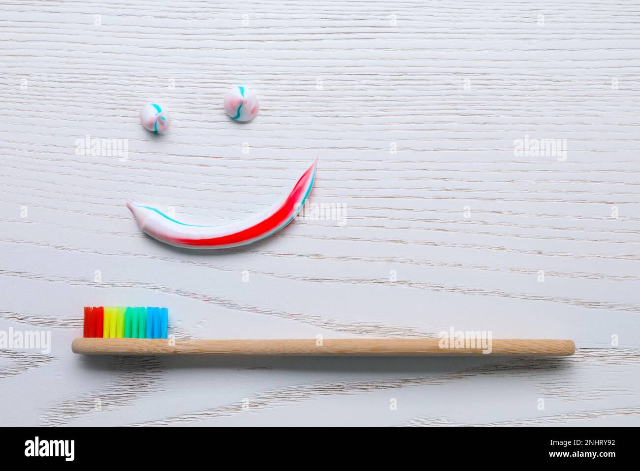 Funny face made with toothpaste and brush on white wooden background ...