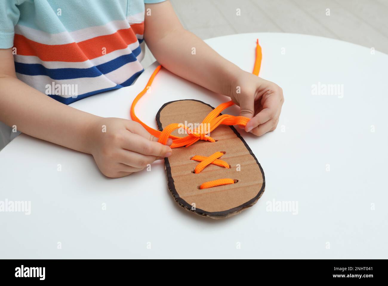 Little boy tying shoe lace using training cardboard template at white ...