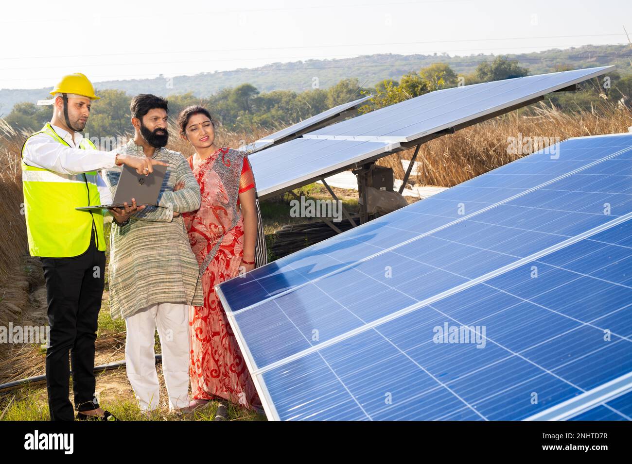 Indian engineer with laptop talking to young couple about solar panel ...
