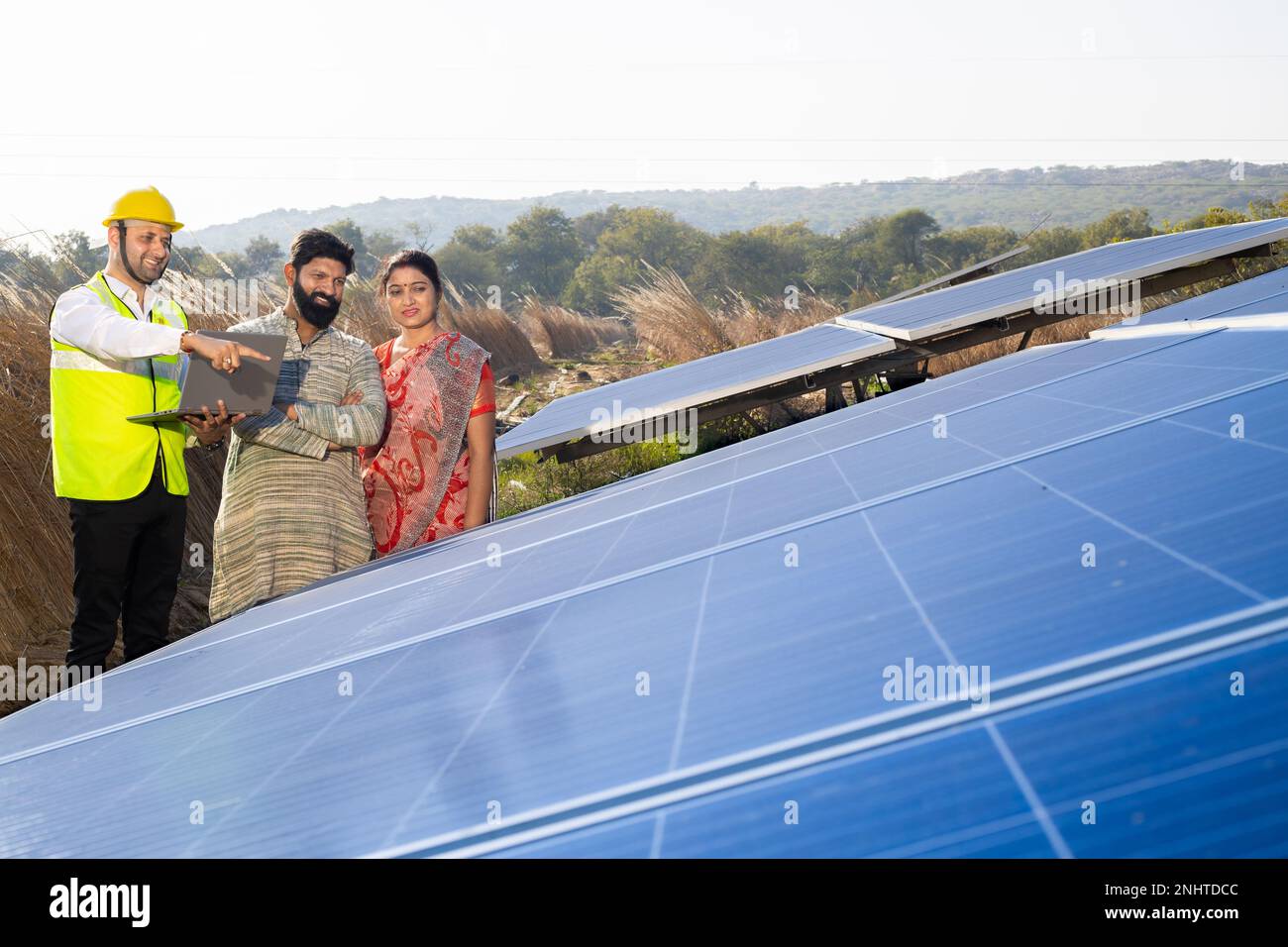 Indian engineer with laptop talking to young couple about solar panel ...