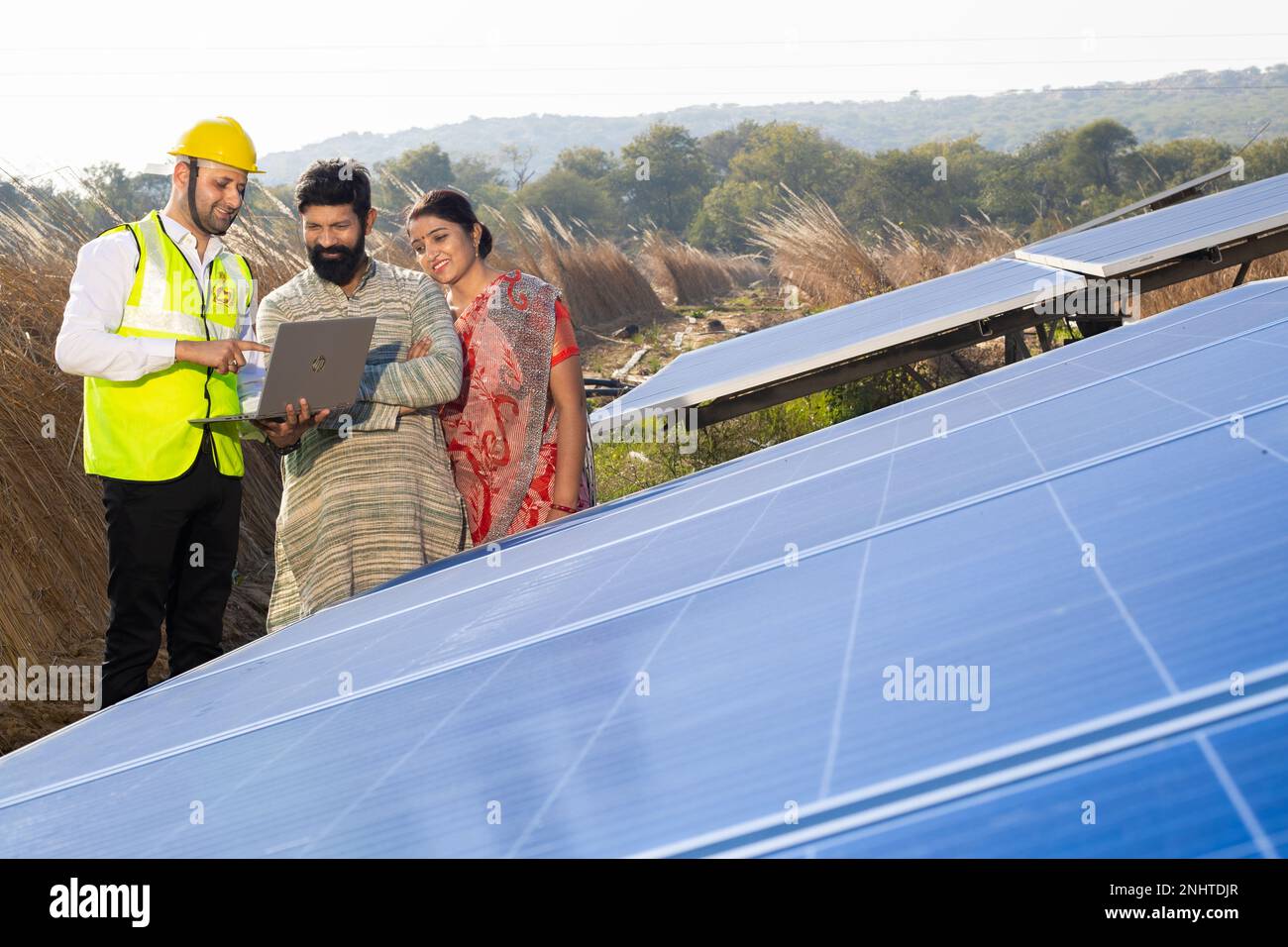 Indian engineer with laptop talking to young couple about solar panel ...