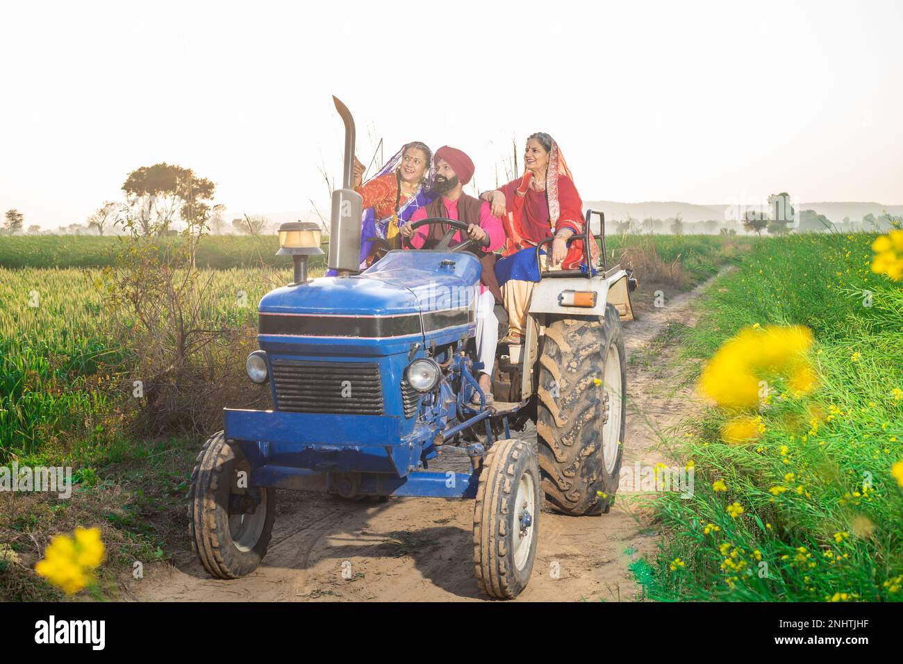 Happy punjabi sikh farmer family driving tractor at agriculture field ...